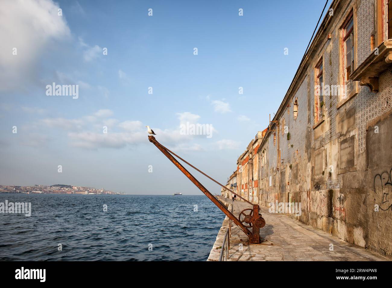Old quay with rusty crane and abandoned buildings by the Tagus river in ...