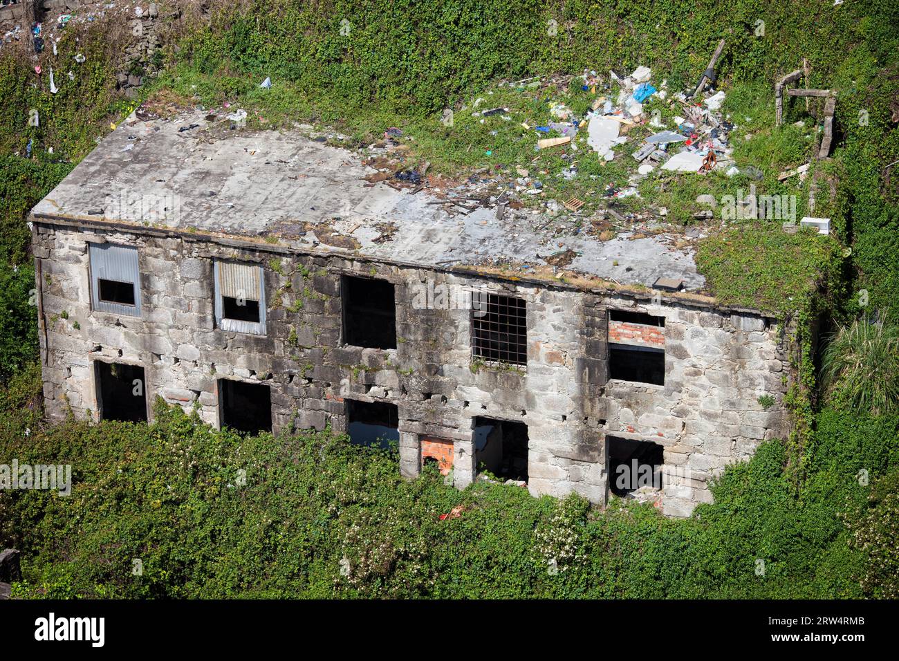 Abandoned old stone building surrounded by lush foliage and trash on a ...