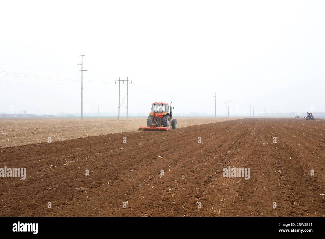 Farmers drive tractors to level up the land for planting corn on the ...
