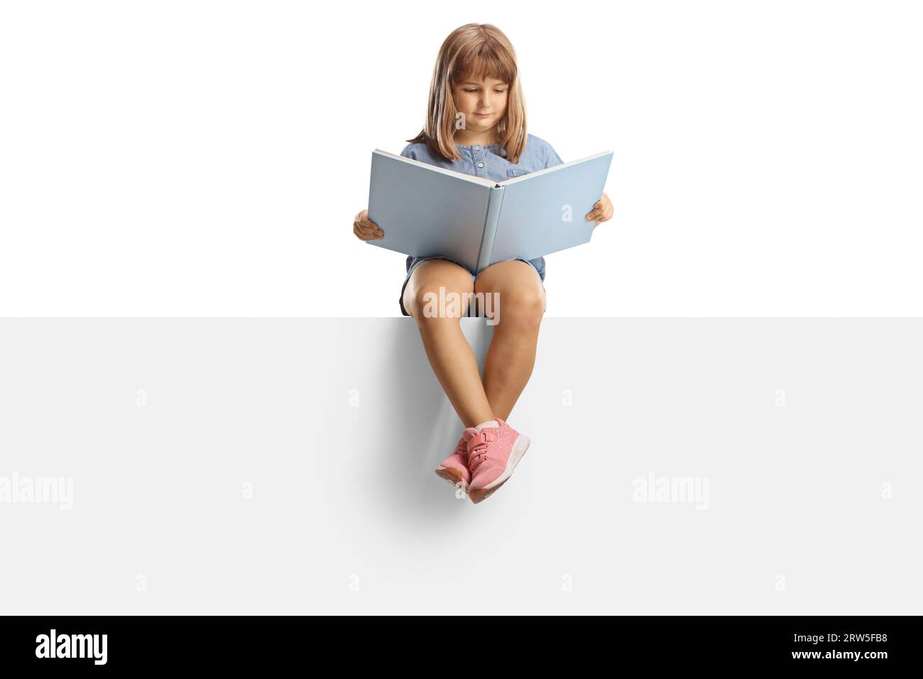 Little girl sitting on a blank panel and reading a book isolated on ...