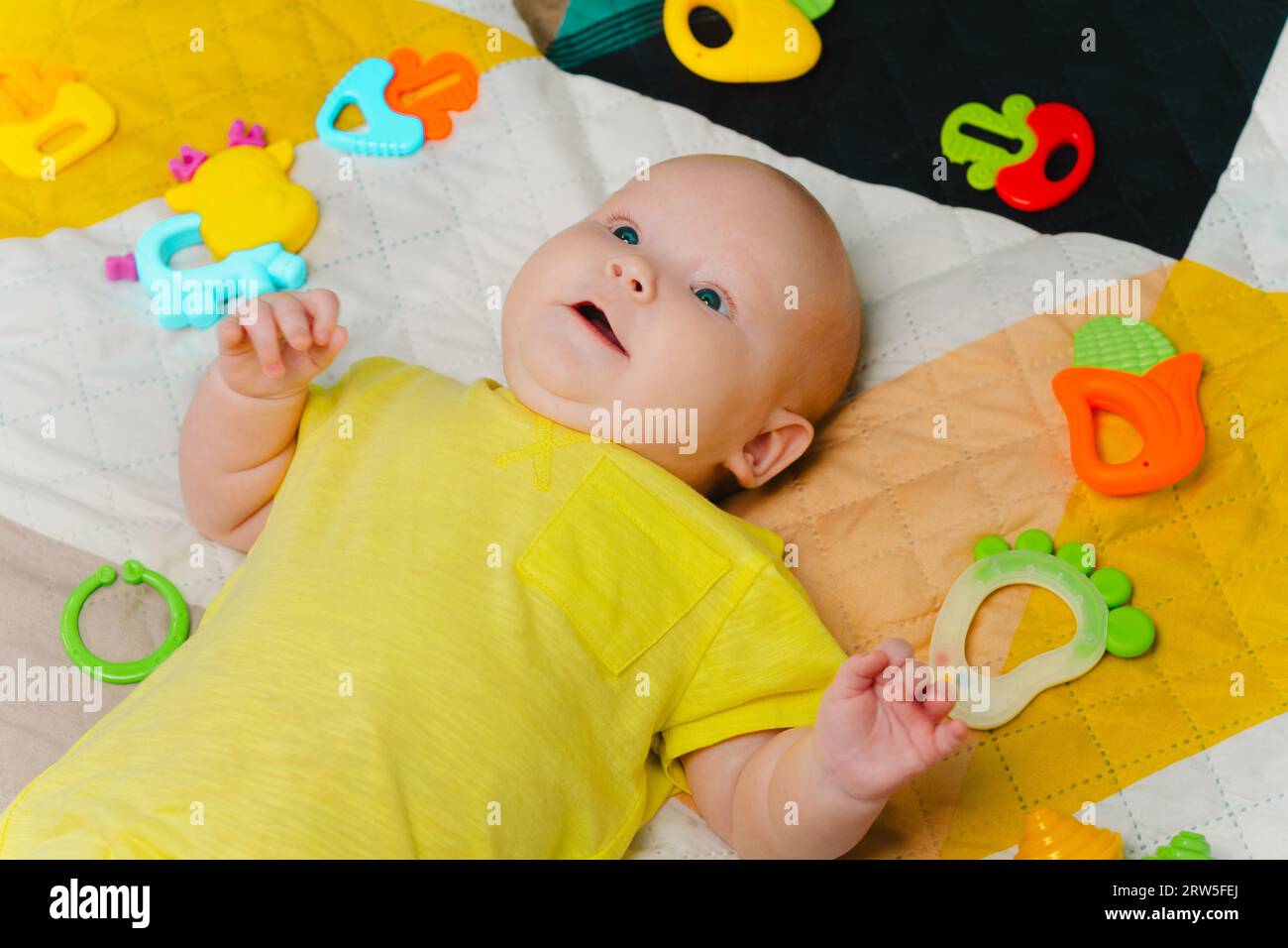 Cute little newborn baby surrounded by colorful toys, lying at home on ...