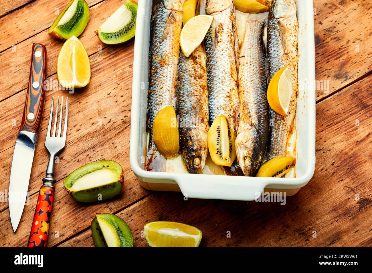 Whole grilled fish with kiwi and lime sauce in baking tray on dark ...