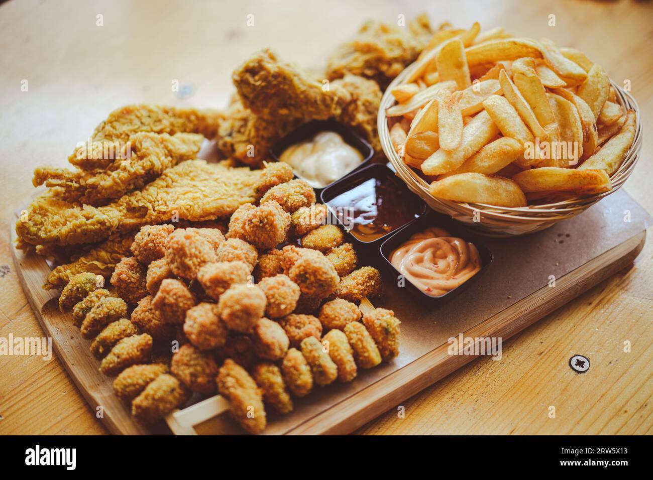 A wooden plateau with various types of fried meat, french fries and ...