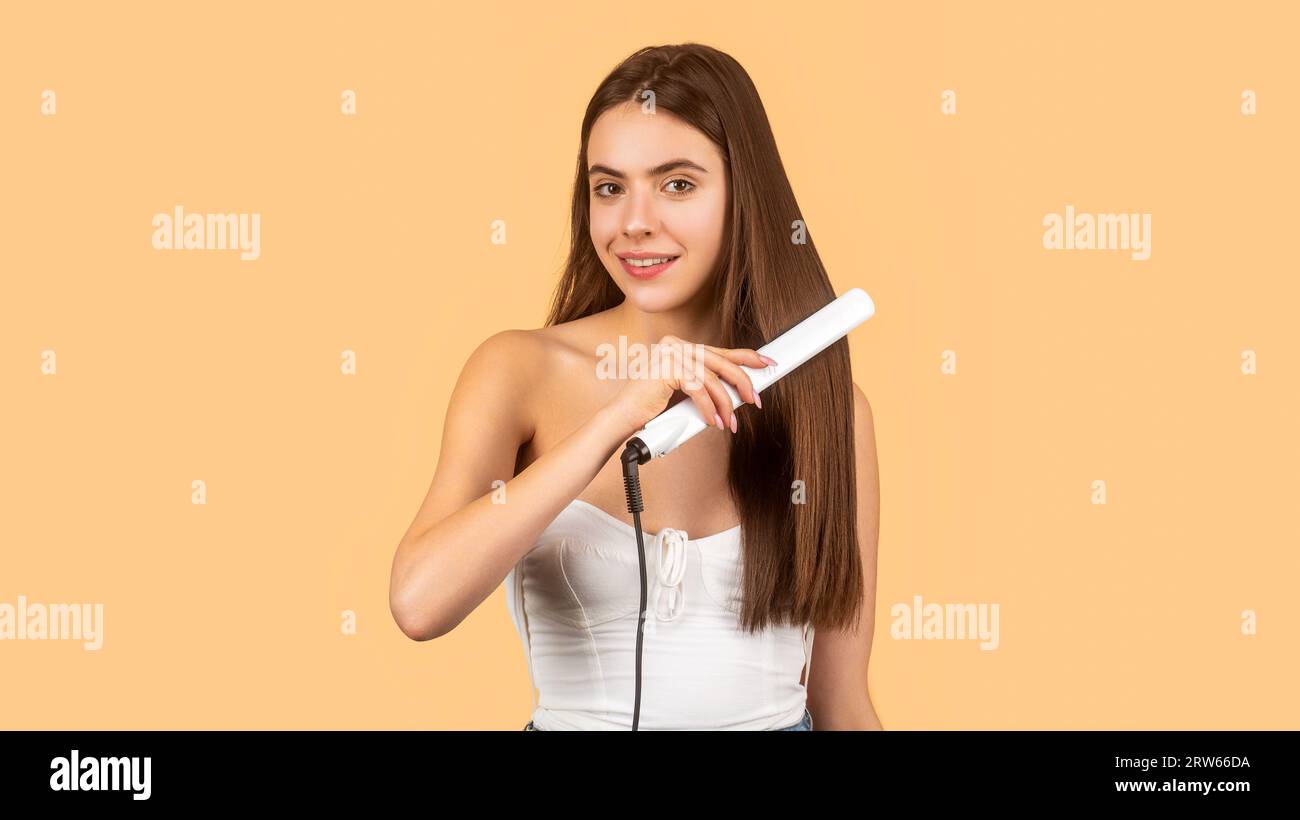 Woman straightening hair with straightener. Portrait of young beautiful ...