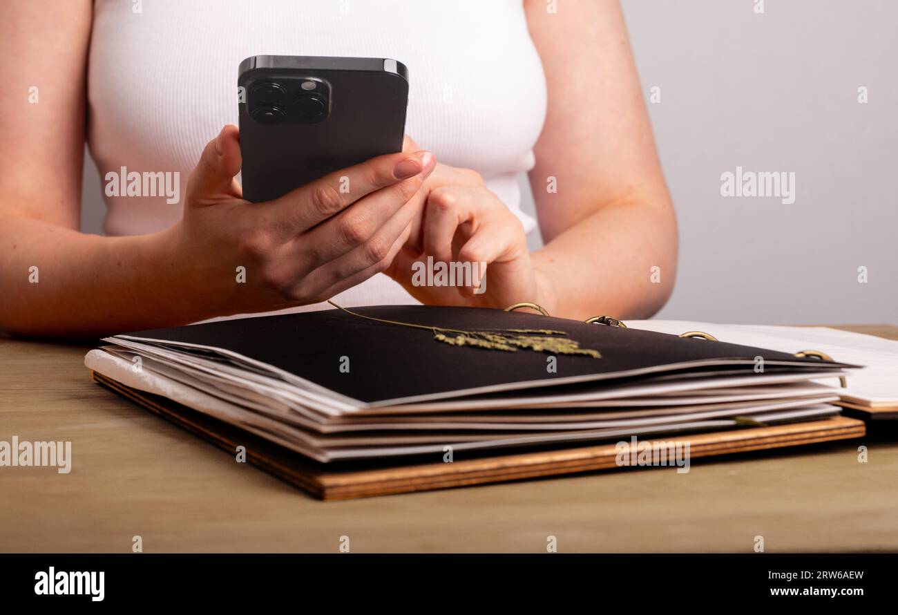 Hands with botany application on smartphone and herbarium book with dry ...