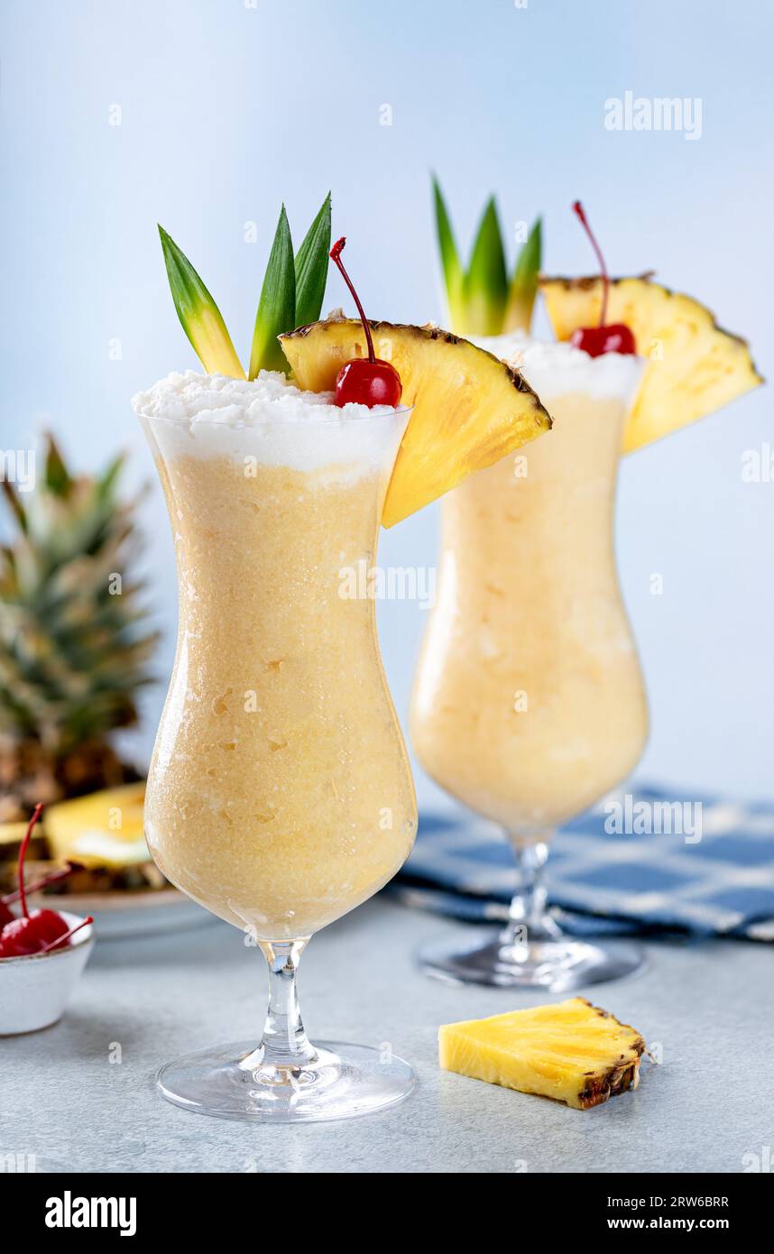 Pina colada cocktails with cherry, pineapple slice and leaves on a blue ...
