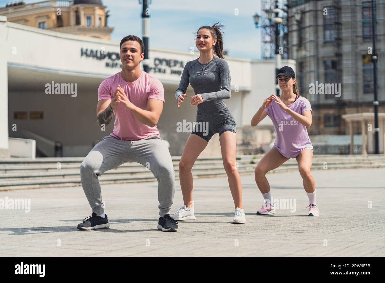 Front view shot of three fit friends doing squats out in the city ...