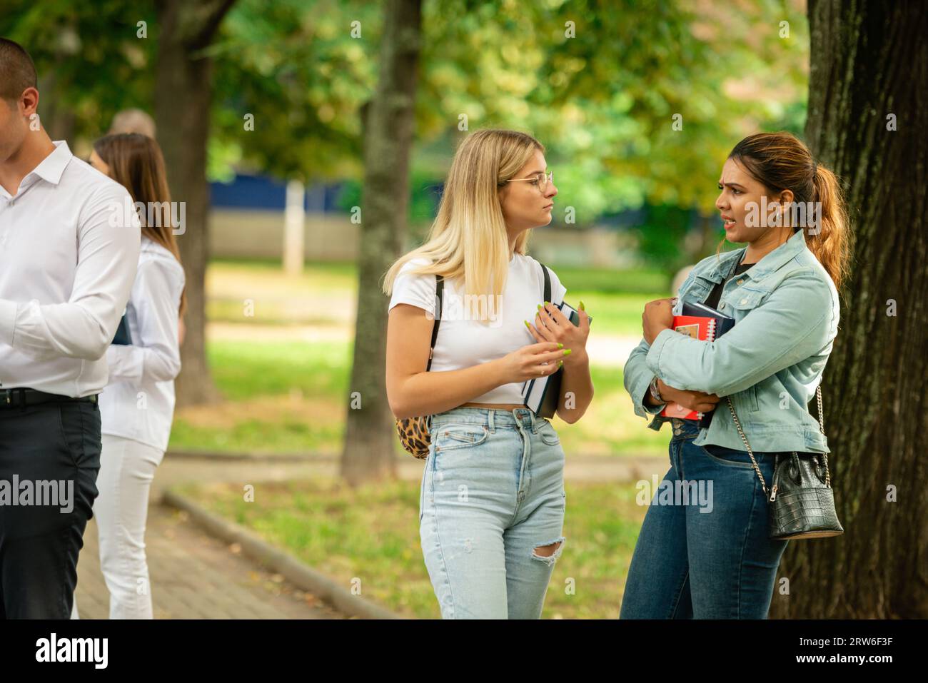 Two multiracial female college campus friends talking to each other ...
