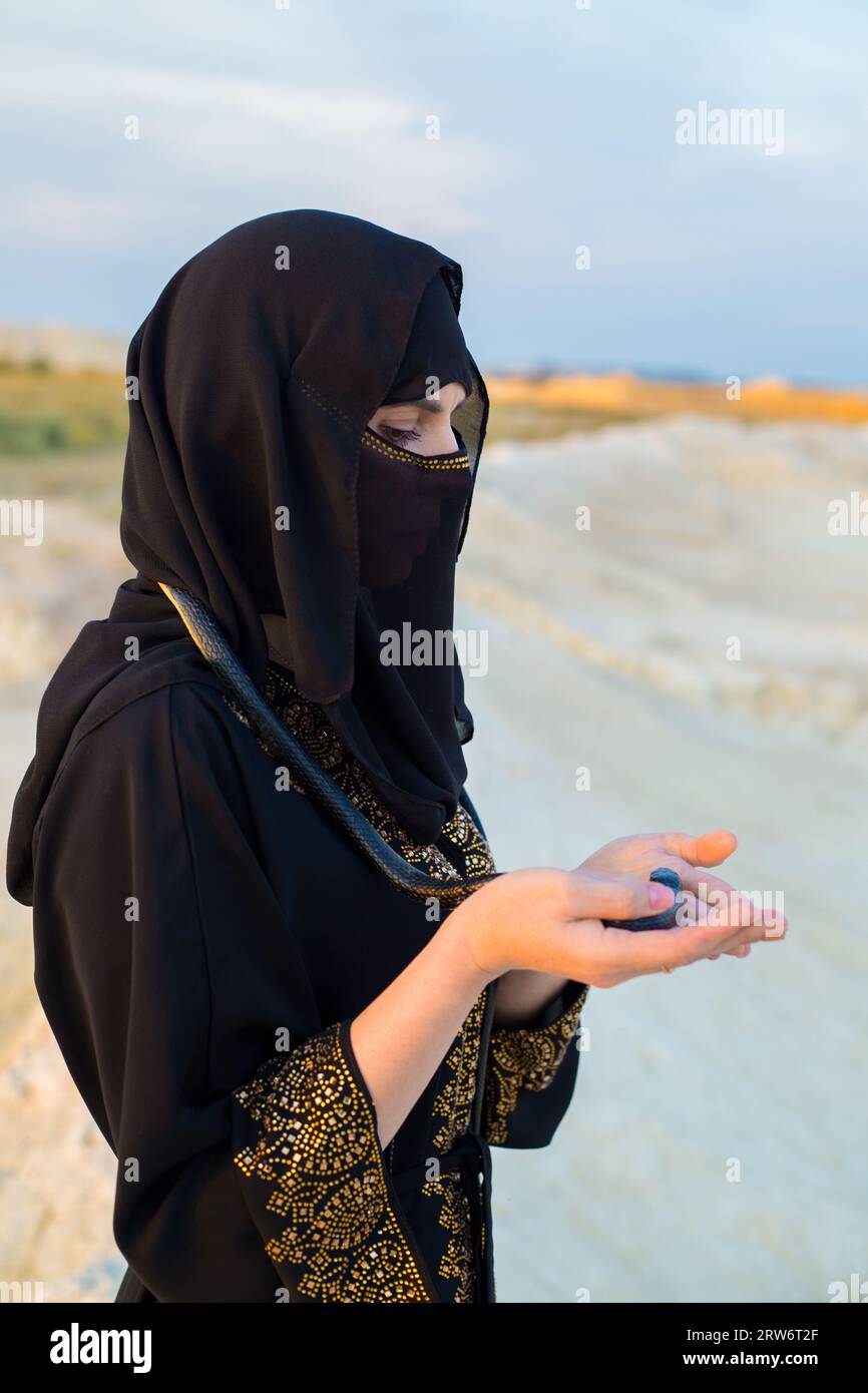 A Muslim woman national dress holds a snake in her hands while standing ...