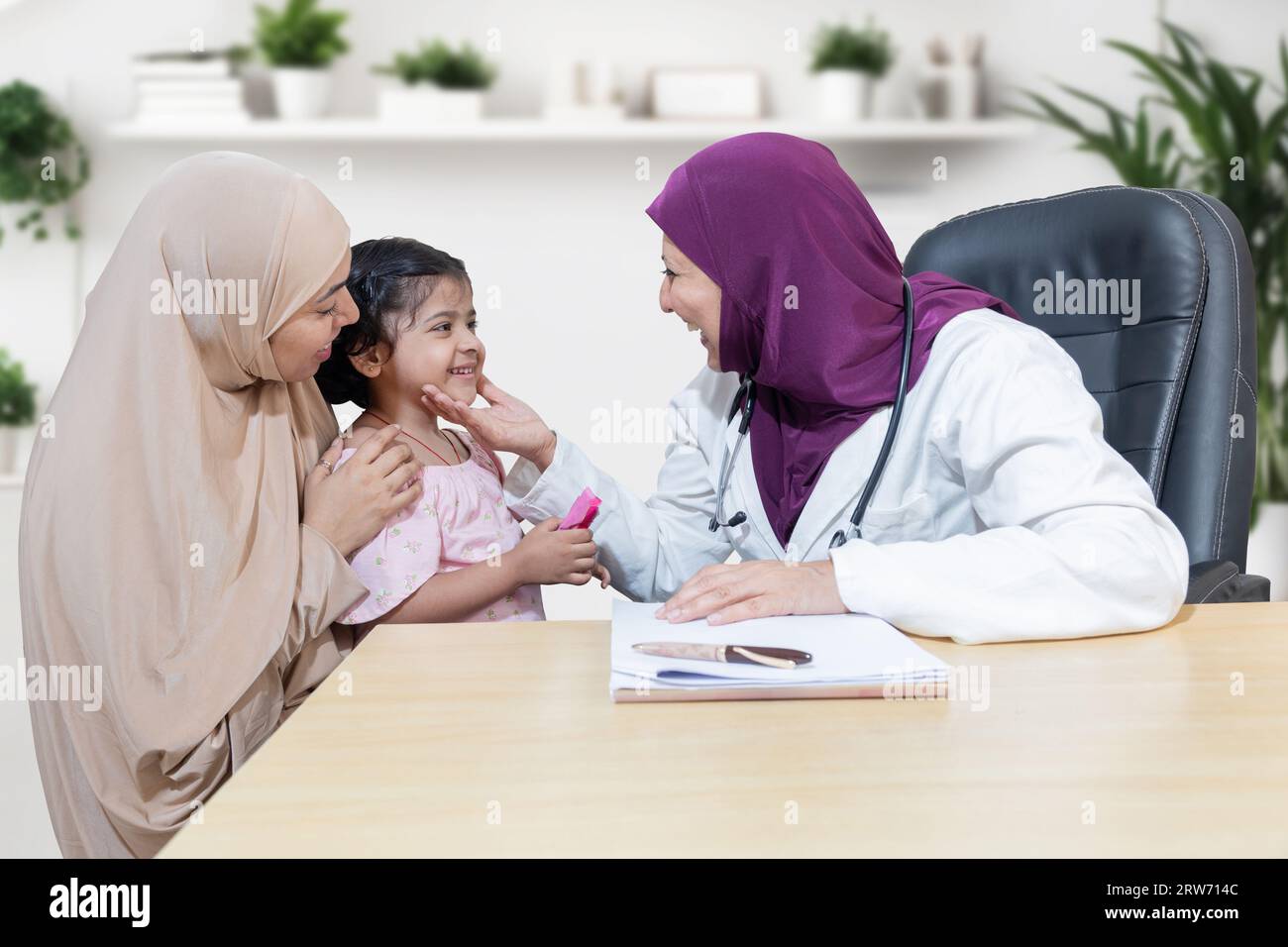Smiling young muslim doctor wearing hijab checking girl child at modern ...