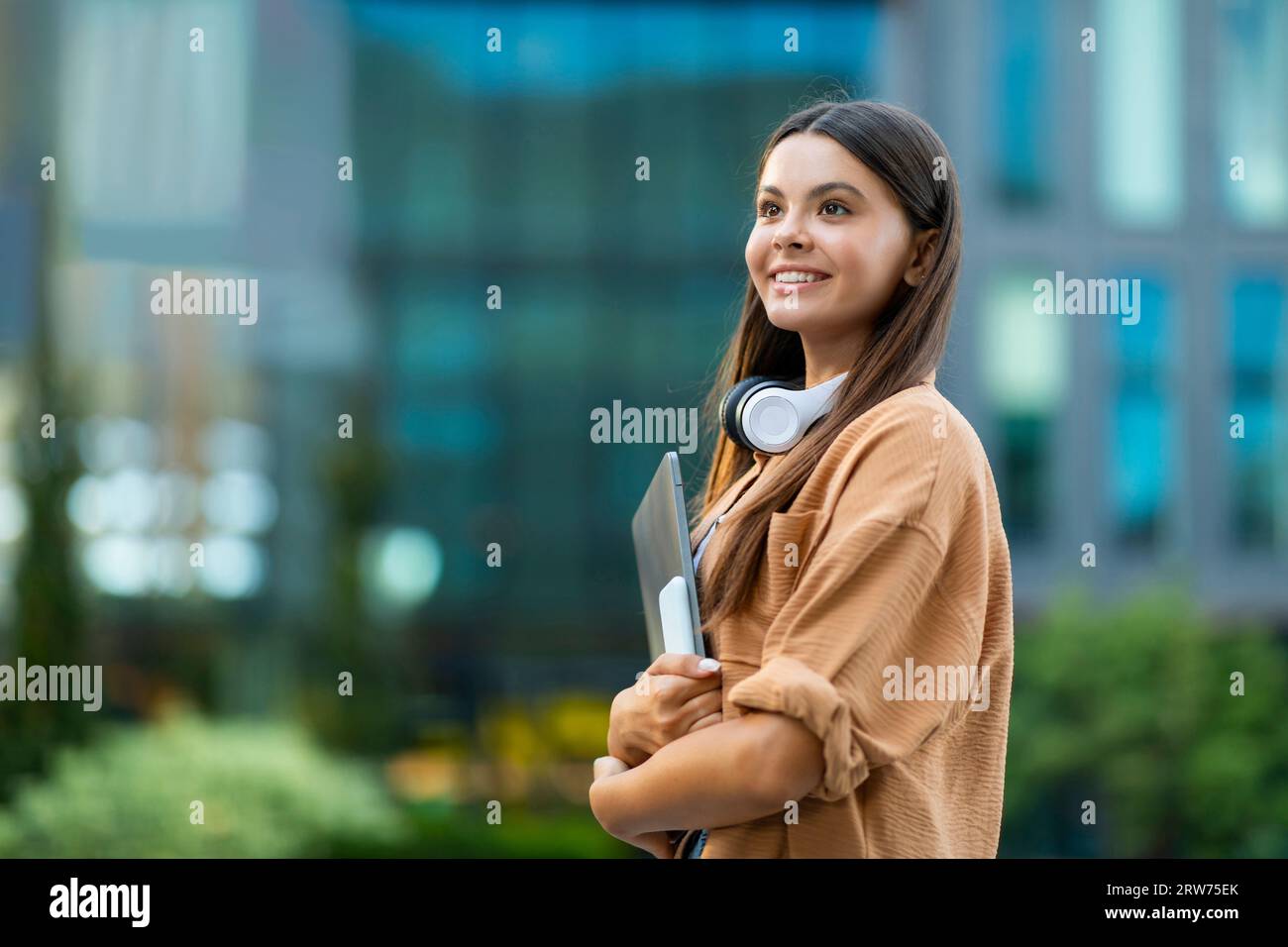 Happy pretty lady student posing at university campus, holding gadgets ...