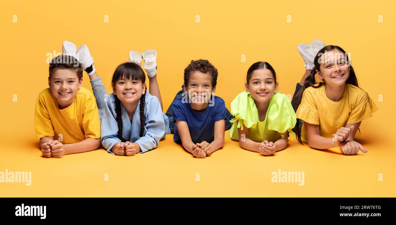 Happy multiracial children lying on floor and smiling, yellow ...