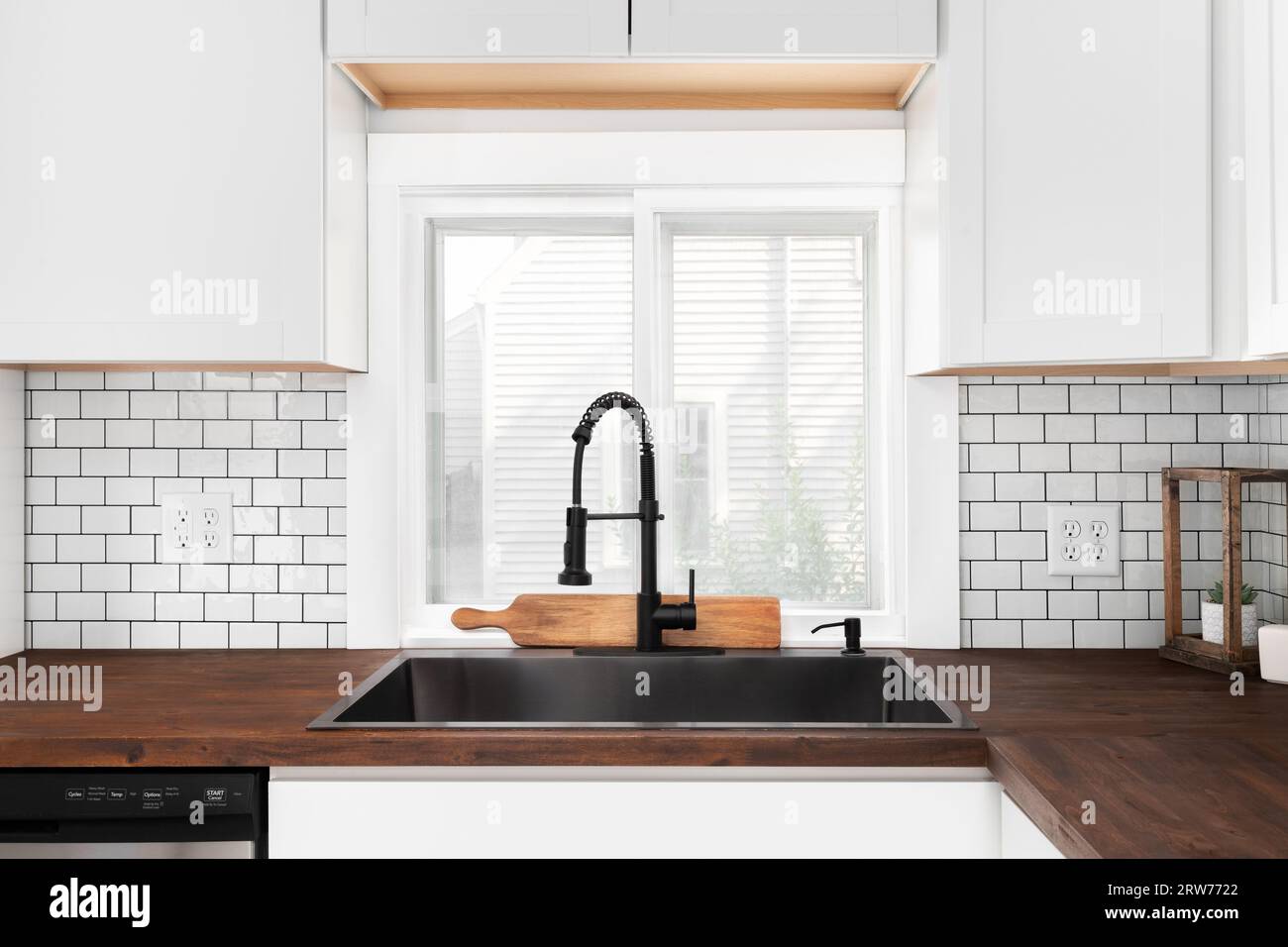 A black kitchen sink and faucet detail in a white kitchen with a ...
