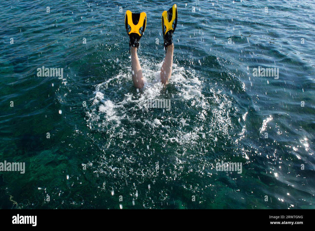 Woman with yellow flippers diving under the blue sea water, splashing ...