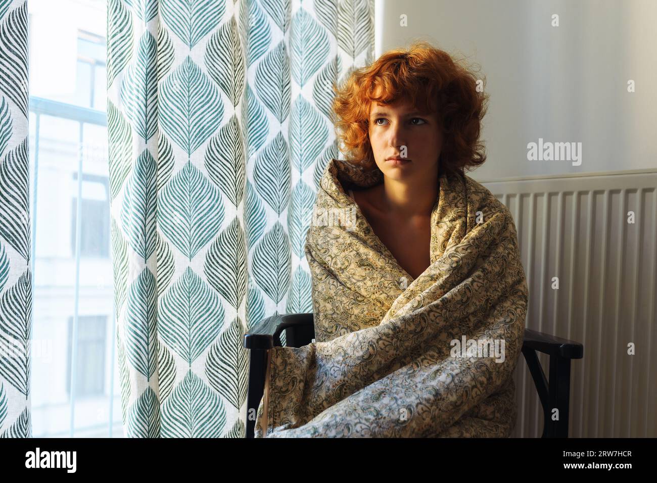 Sleepy teenage girl, in blanket, sitting on chair near radiator Stock ...