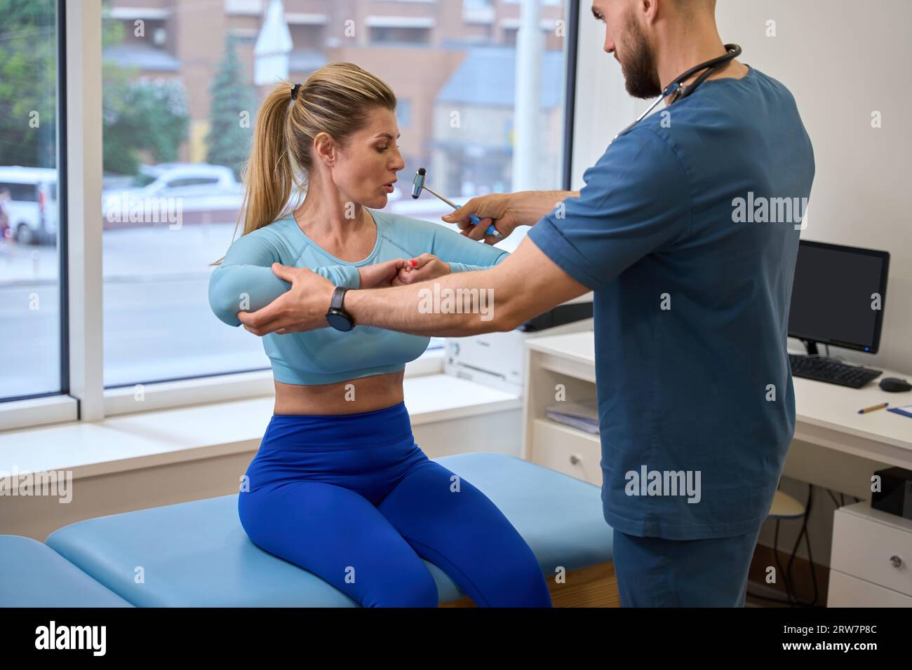 Concentrated doctor neurologist checking reflexes of sportive woman ...