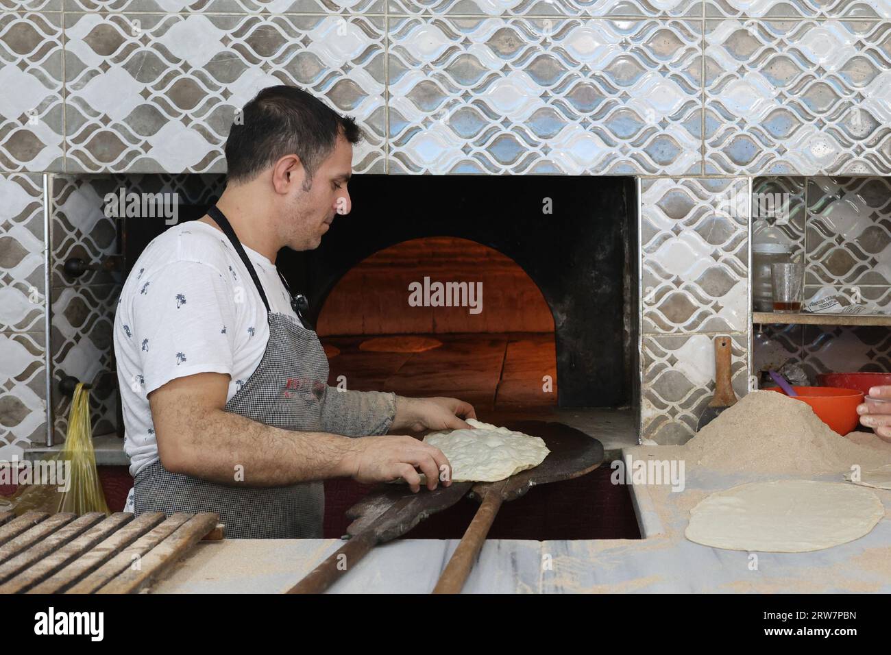 A baker making Turkish flatbread to be baked in an oven kiln, in ...