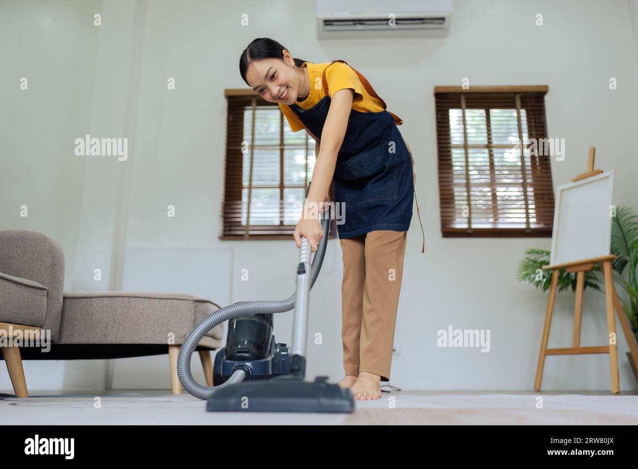 Beautiful young girl housekeeper cleaner wear apron and vacuuming messy ...