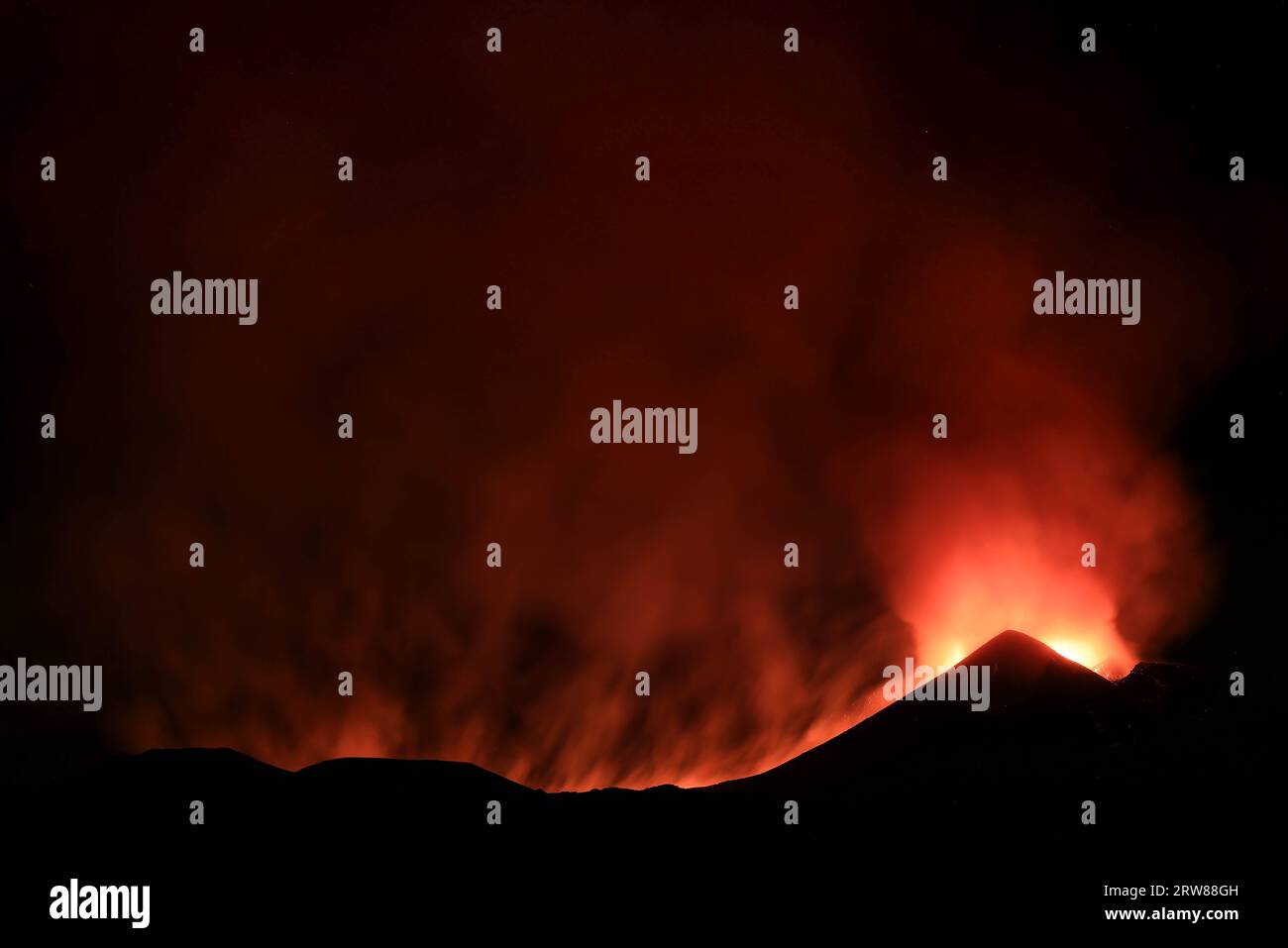 Etna in a nocturne lava eruption with backlight silhouette crater and large smoke emissions in a ...