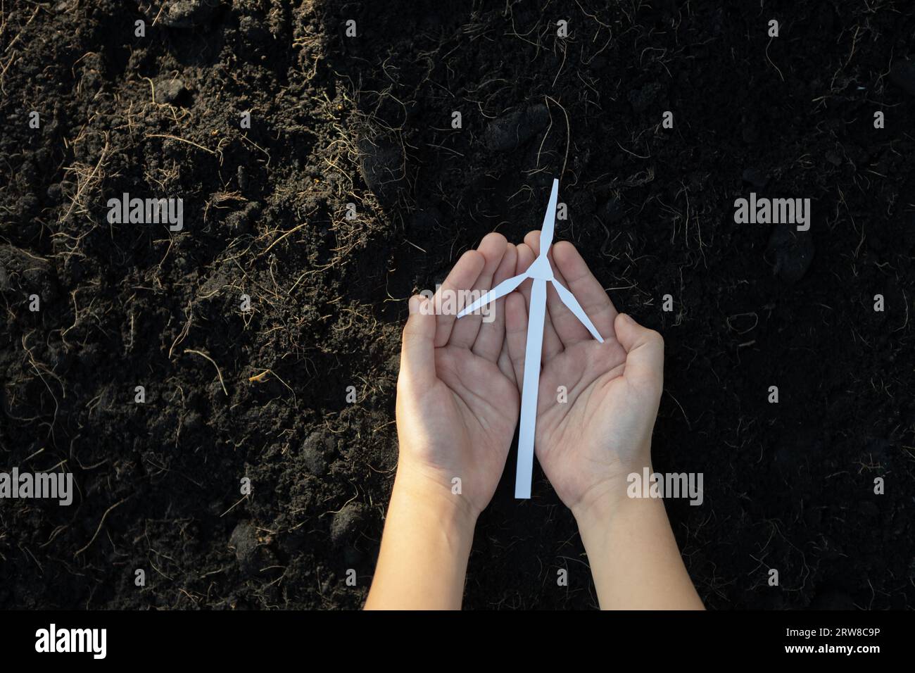 Hand holding wind turbine mockup or model over soil background top view ...