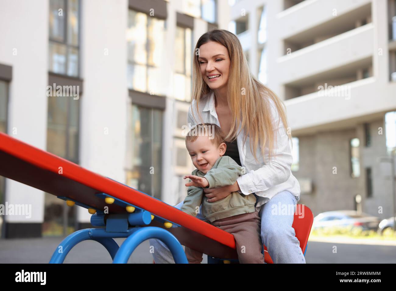 Happy nanny with cute little boy on seesaw outdoors Stock Photo - Alamy