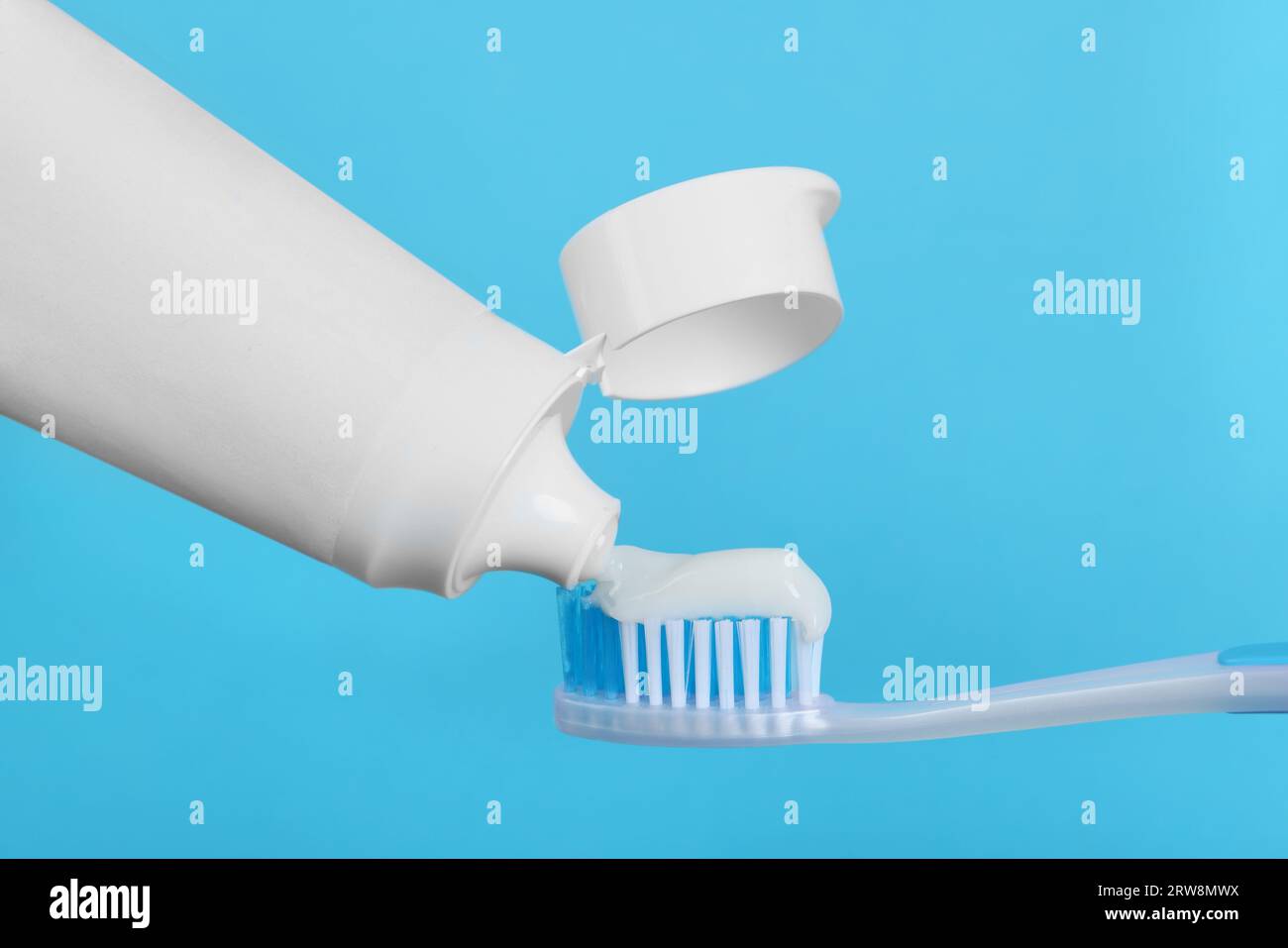 Applying paste on toothbrush against light blue background, closeup ...