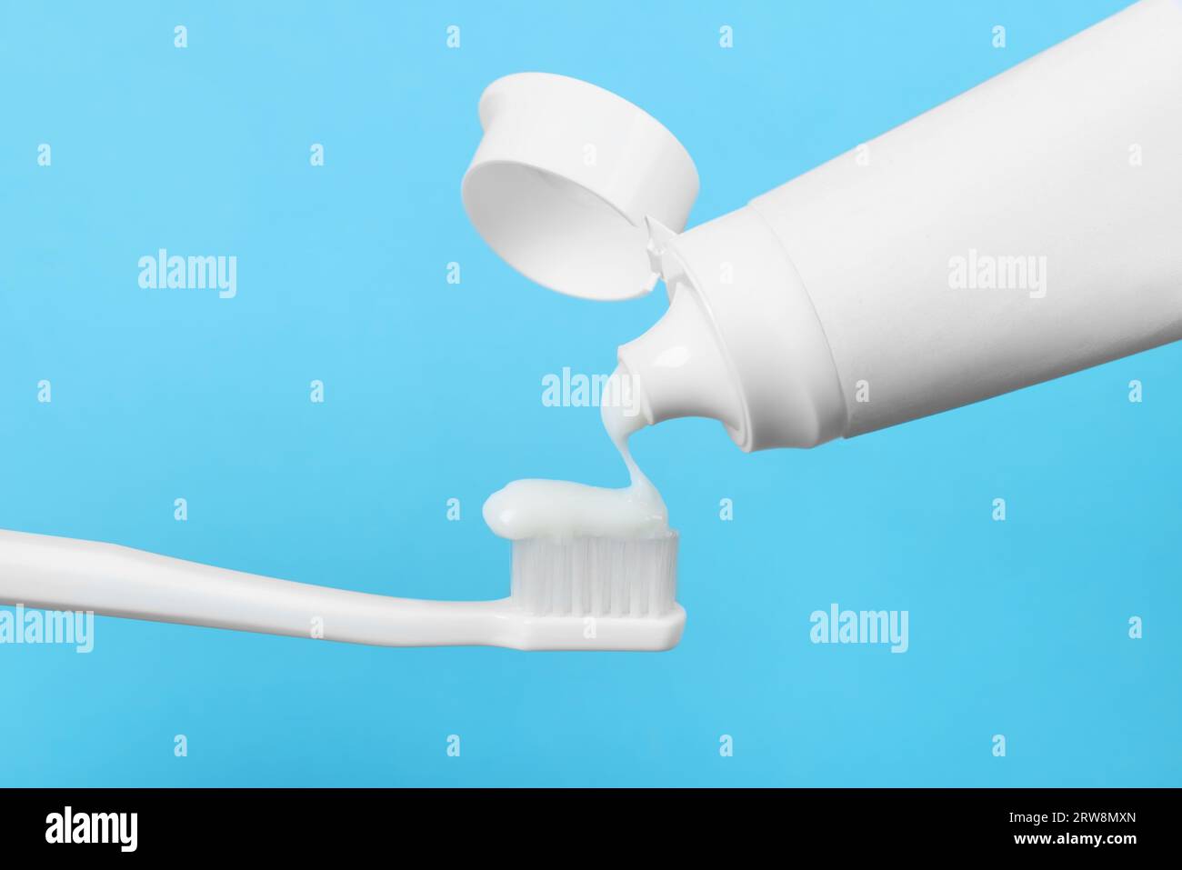 Applying paste on toothbrush against light blue background, closeup ...