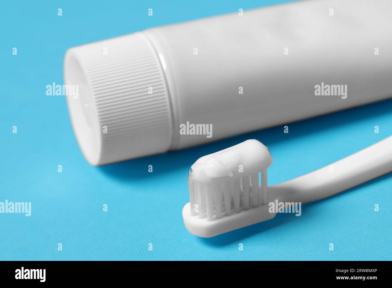 Plastic toothbrush with paste and tube on light blue background ...
