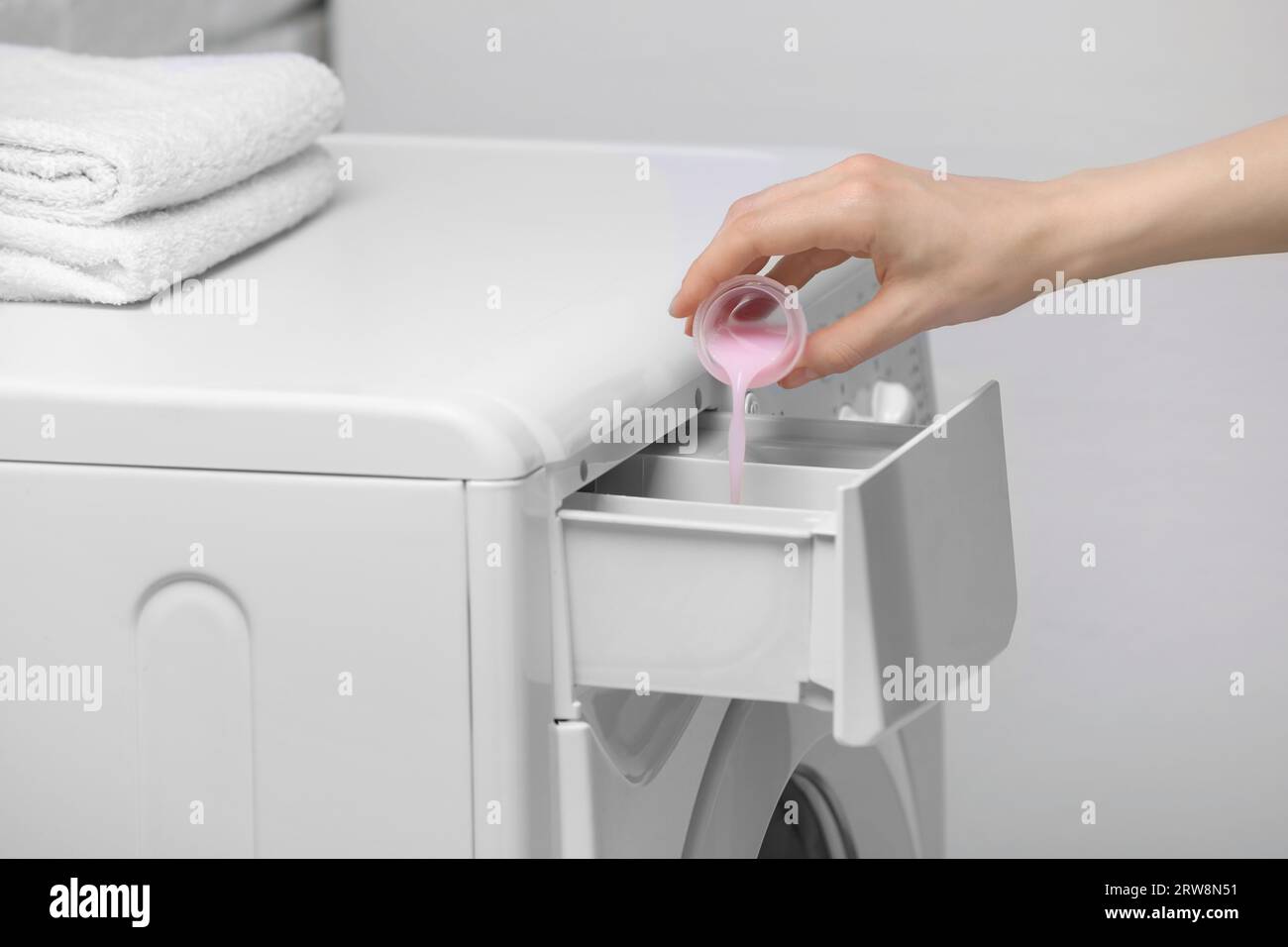 Woman pouring fabric softener from cap into washing machine on light ...