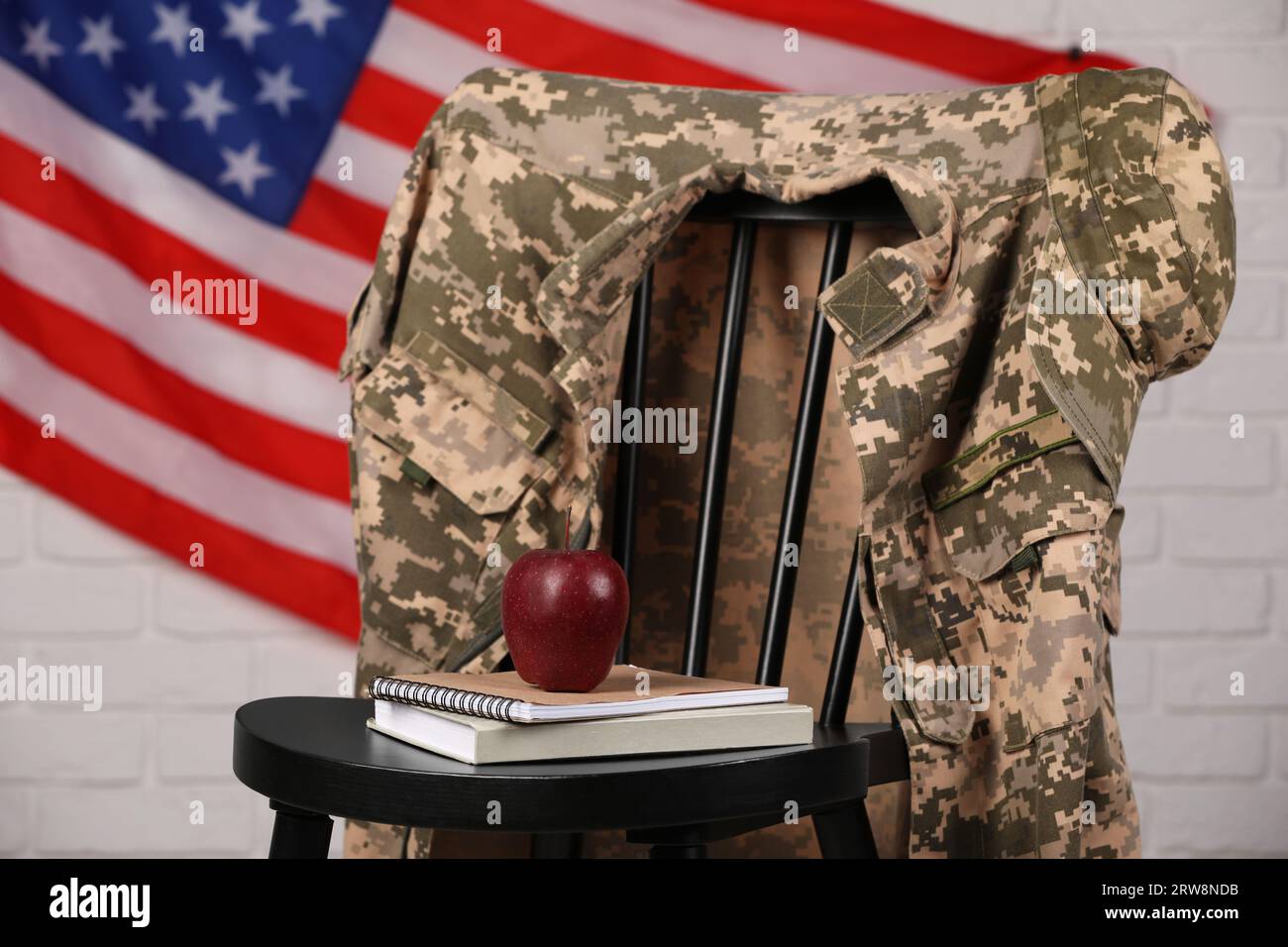 Soldier uniform, notebooks and apple on chair near flag of United ...