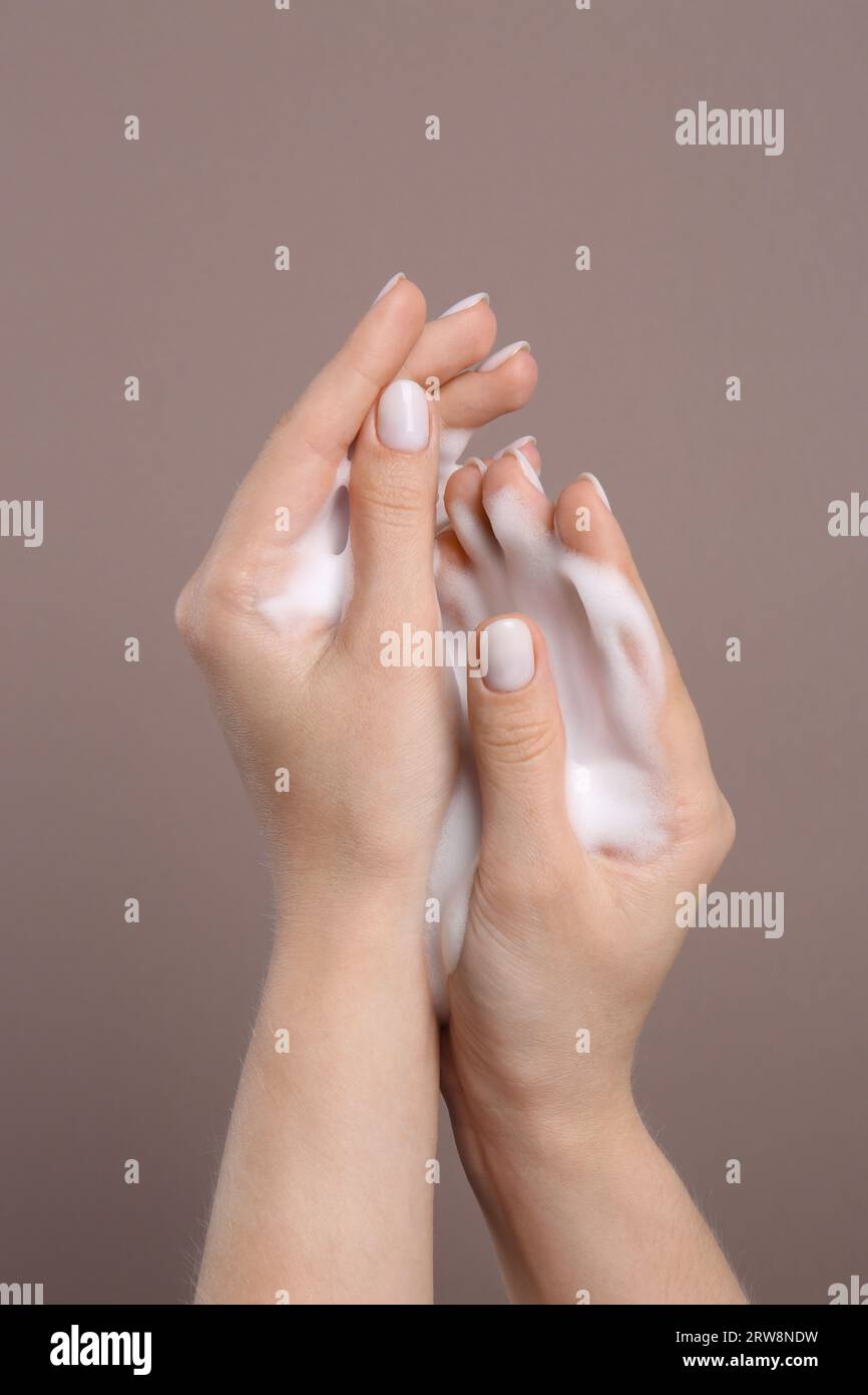 Woman washing hands with cleansing foam on brown background, closeup ...