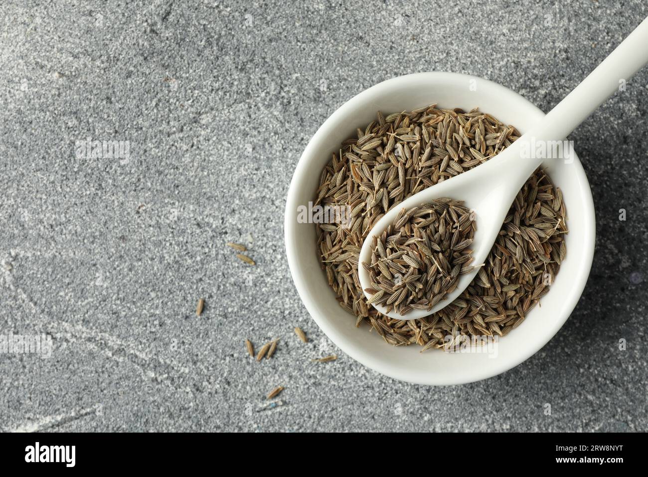 Bowl of caraway (Persian cumin) seeds and spoon on gray textured table ...