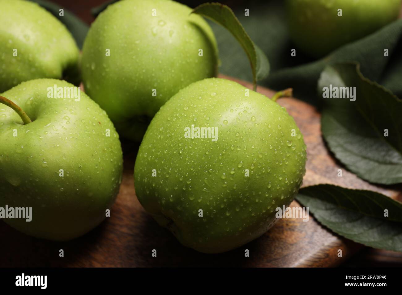 Ripe green apples with leaves and water drops on wooden board, closeup ...