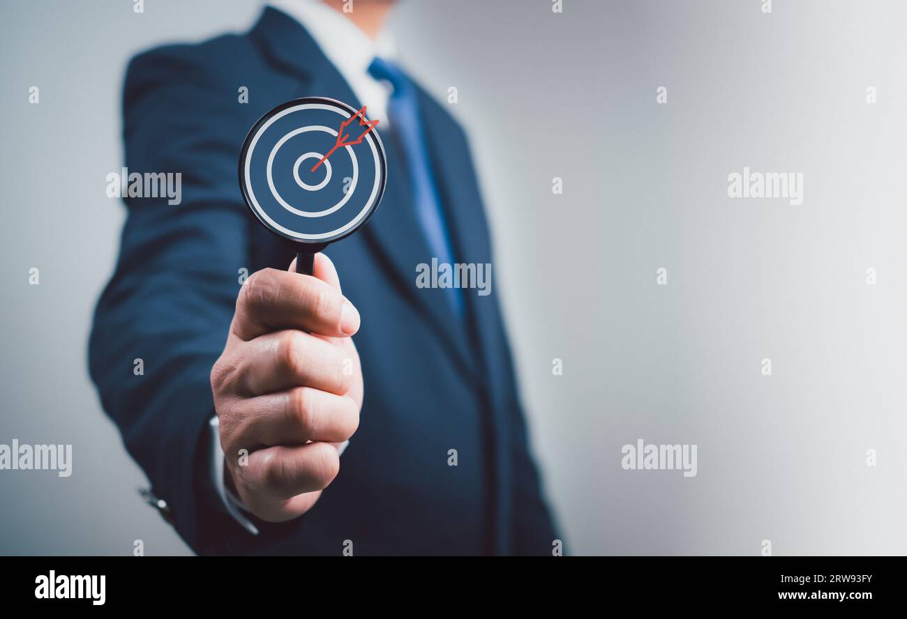 Businessman's hand is holding a magnifying glass showing a target icon ...