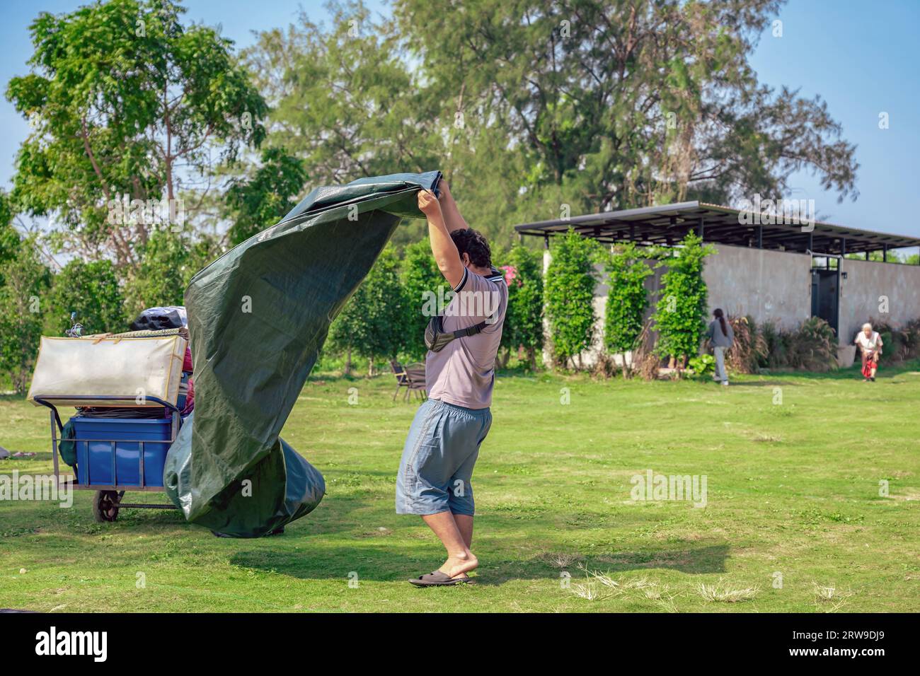 Back view of Asian man clean and collect tarps used to set up their ...