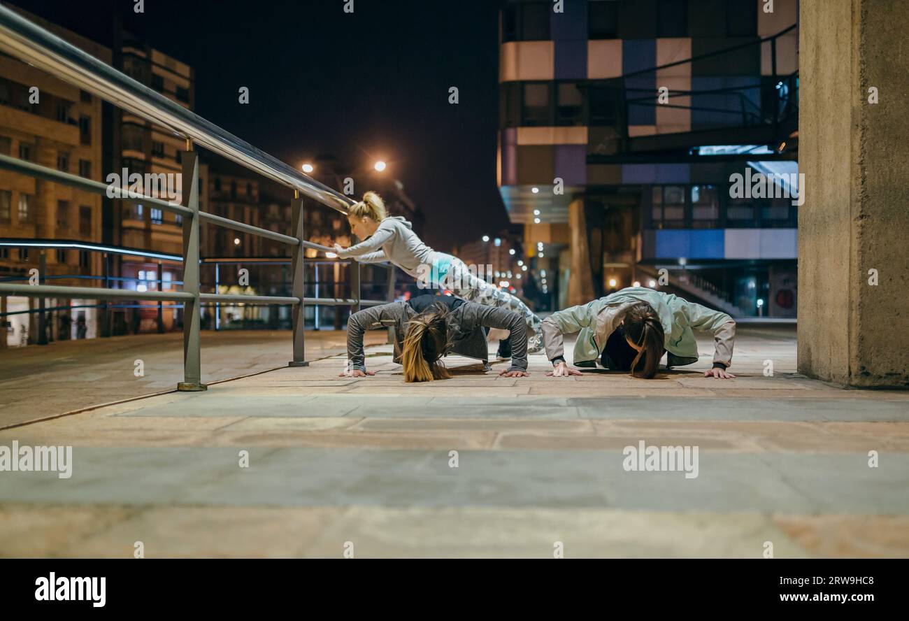 Female sport team doing push ups during training on the city at night ...