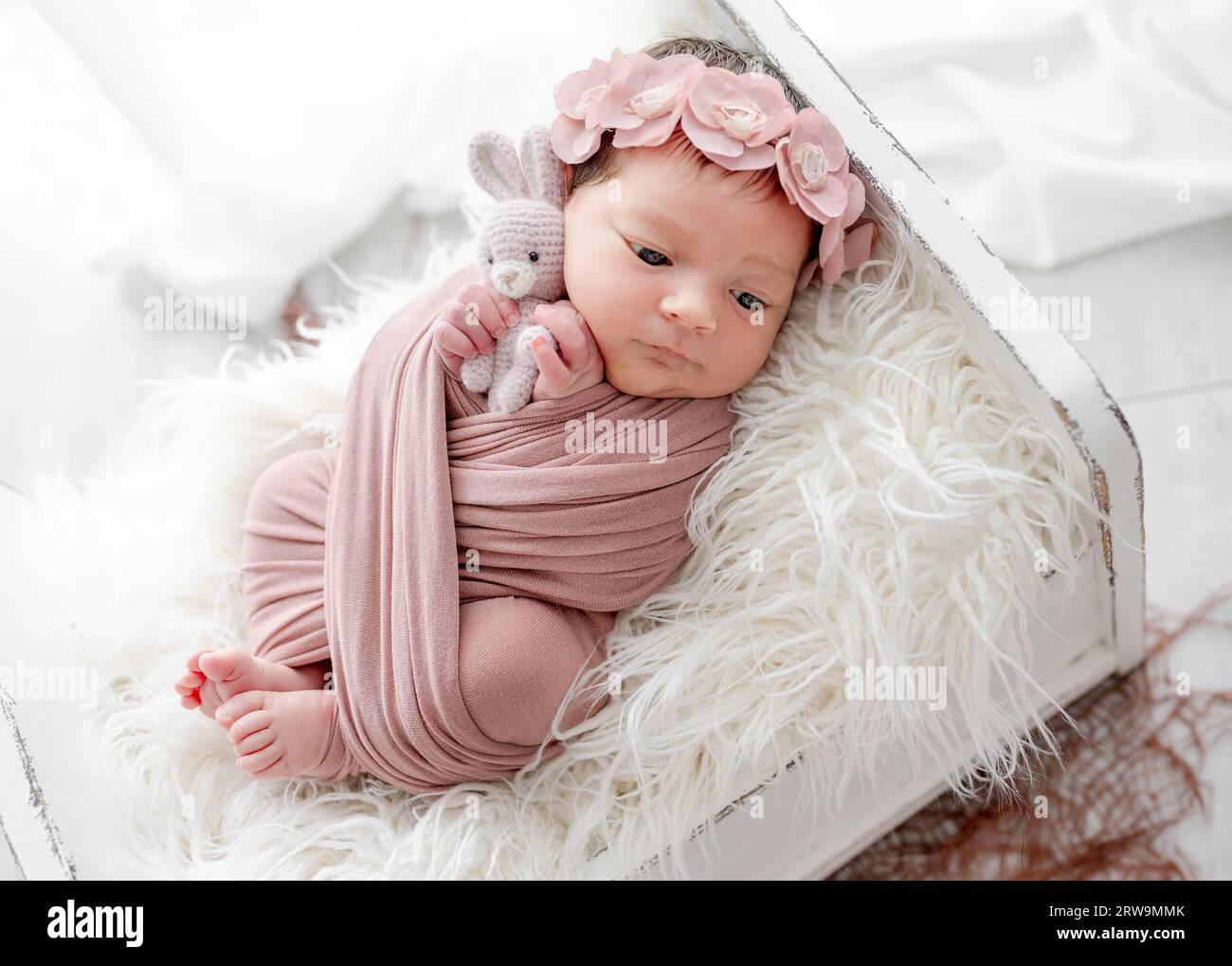 Adorable newborn baby girl lying in tiny bed on fur portrait. Cute infant child kid swaddled in ...