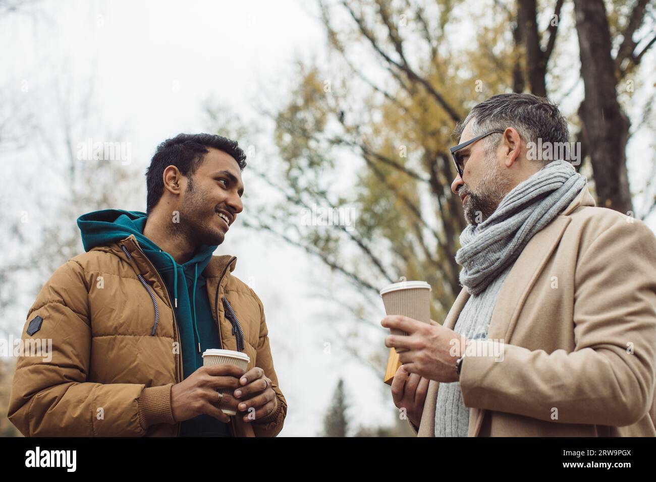 Friends, a senior and a young man walking and talking and drinking ...