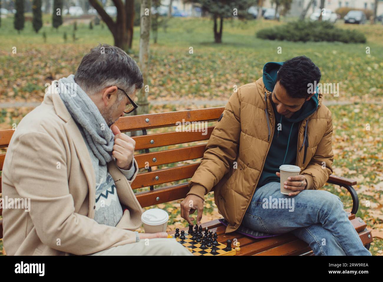 Friends play chess on a bench in an autumn park. Multicultural ...