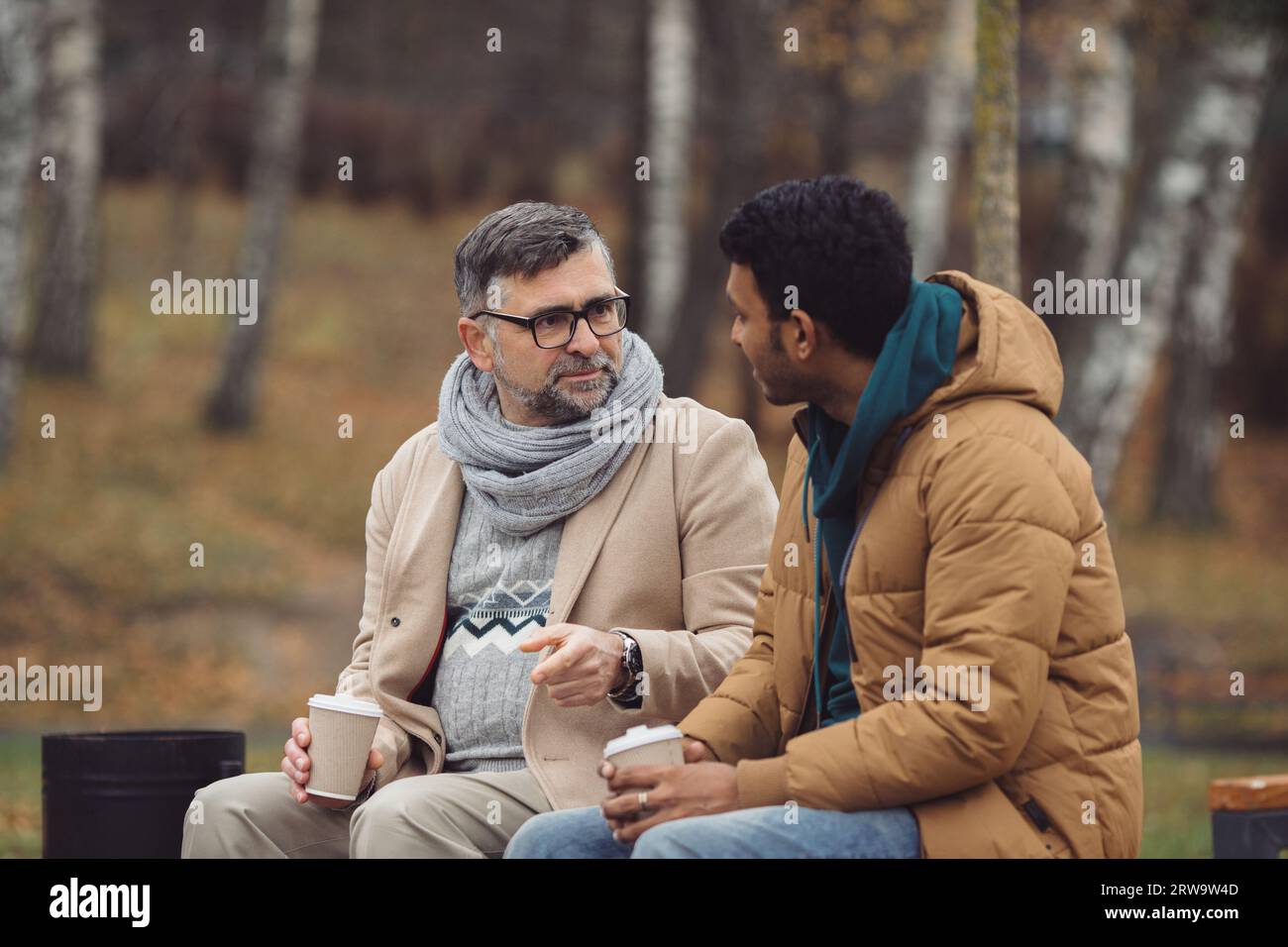 Friends, a senior and a young man sit in the park on a bench and talk ...