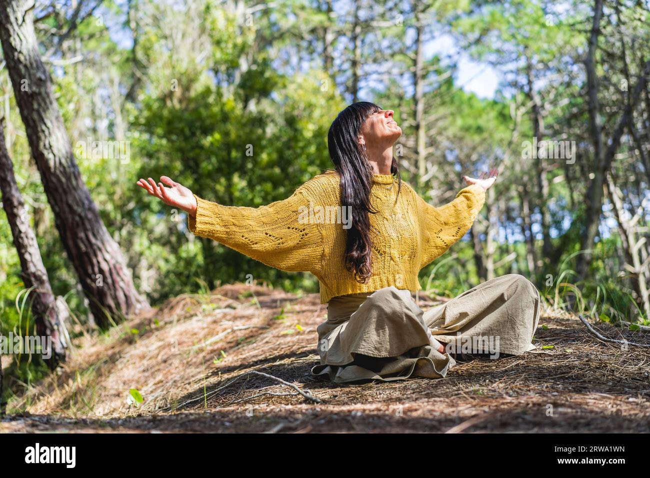 Woman sitting on the woods with arms opened while looking to the sky ...