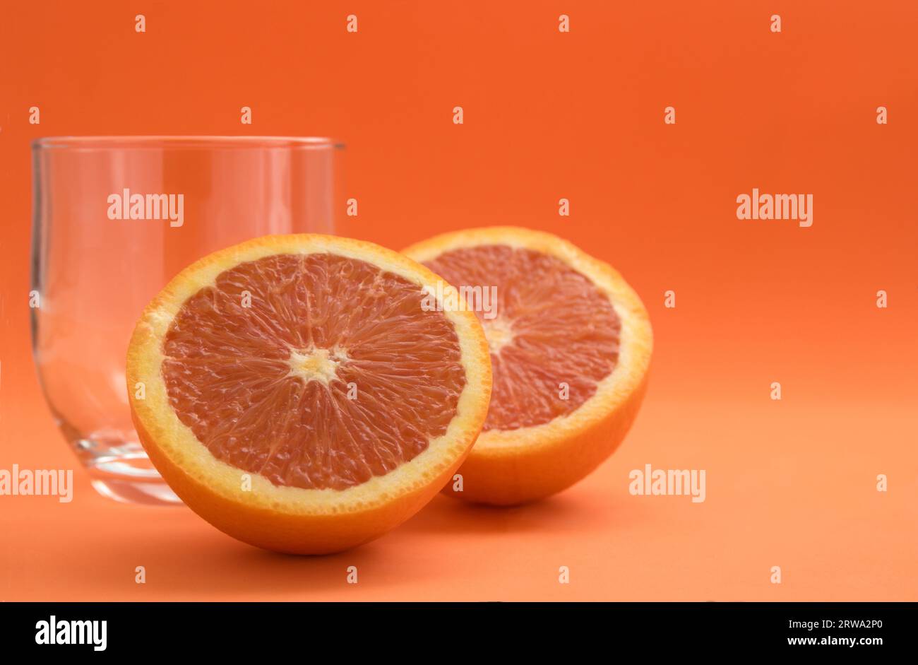 Closeup of a red orange cut in half next to a glass glass on an orange ...