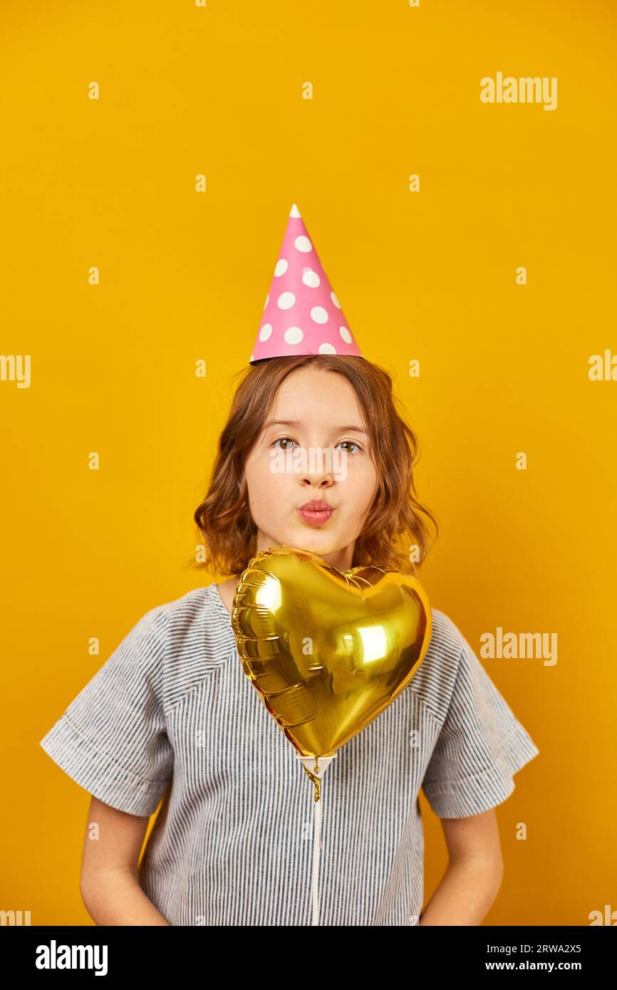 Cheerful, positive ten years birthday girl in party hat with balloons ...