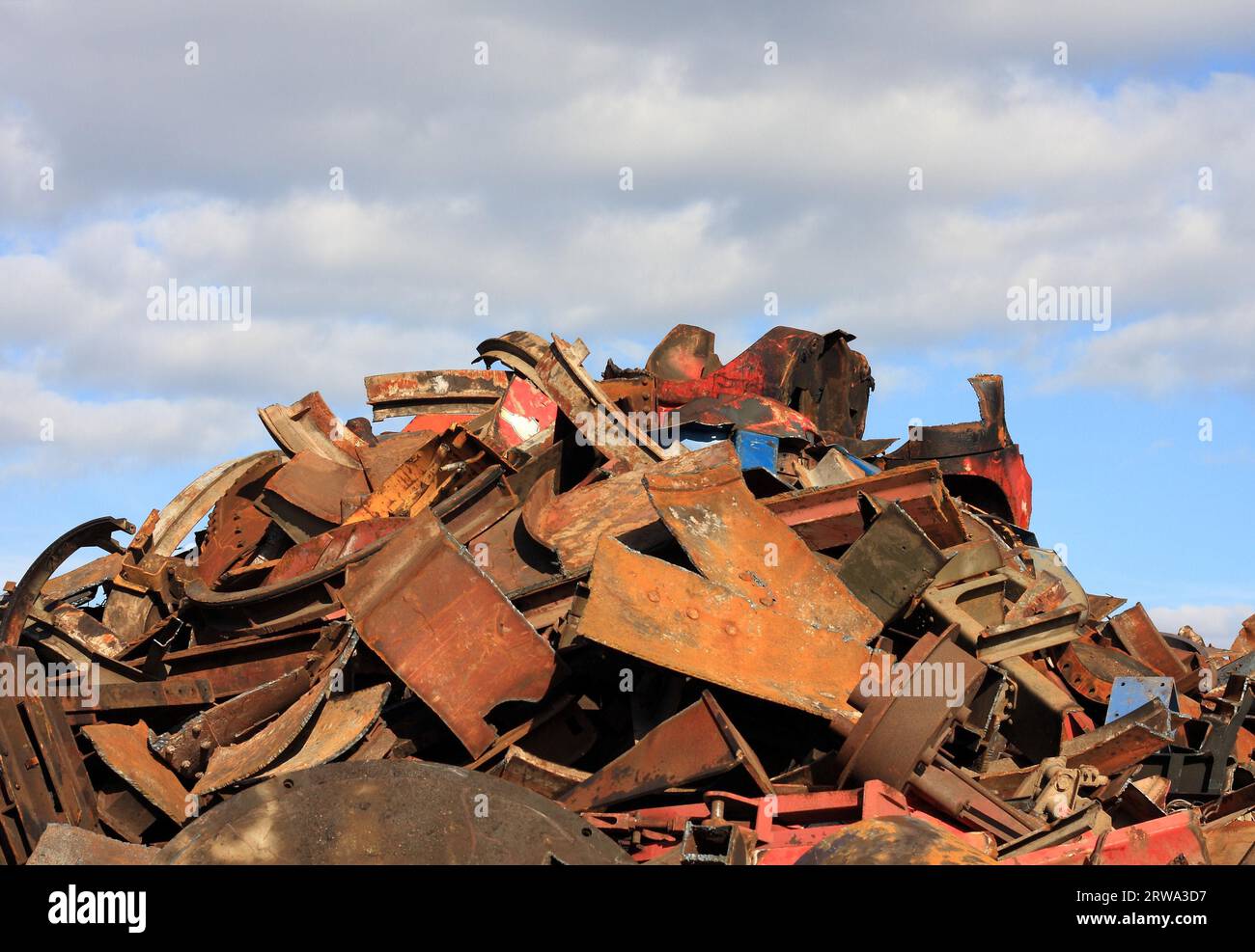 Piled up scrap iron and steel, background blue sky and white clouds ...