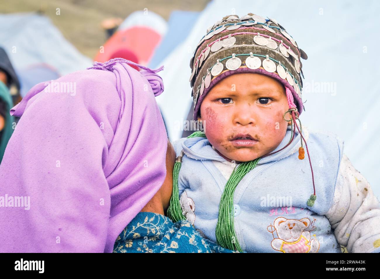 Dolpo, Nepal, circa May 2012: Small child in blue sweater with green necklace and cap with coins ...