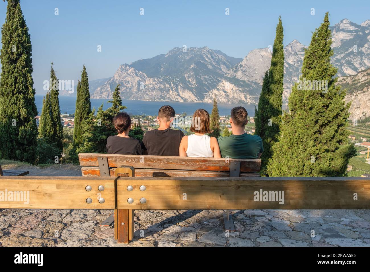 Rear view of four people sitting on bench against lake and mountains ...