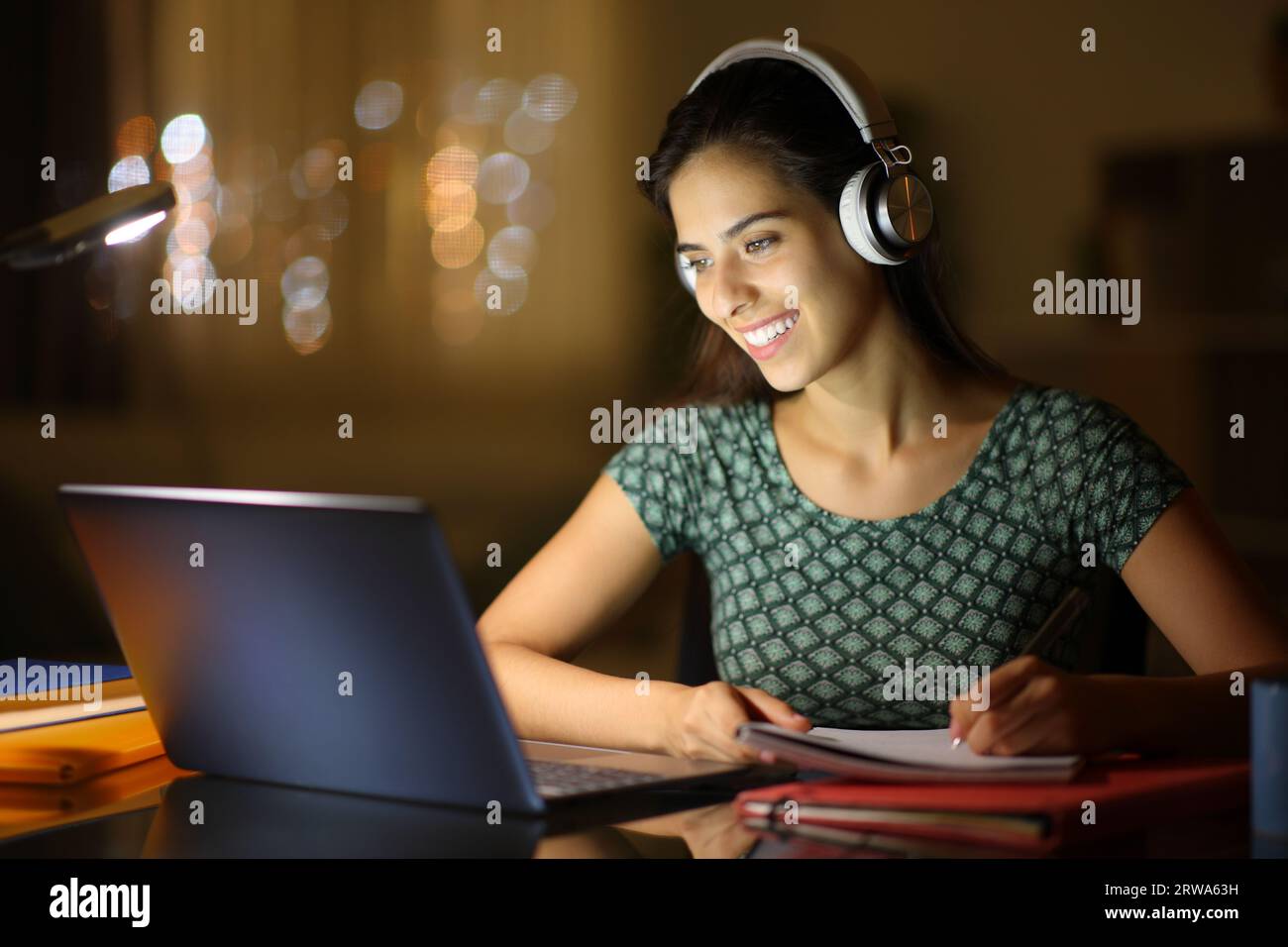 Happy student in the night elearning with laptop and headphone at home ...