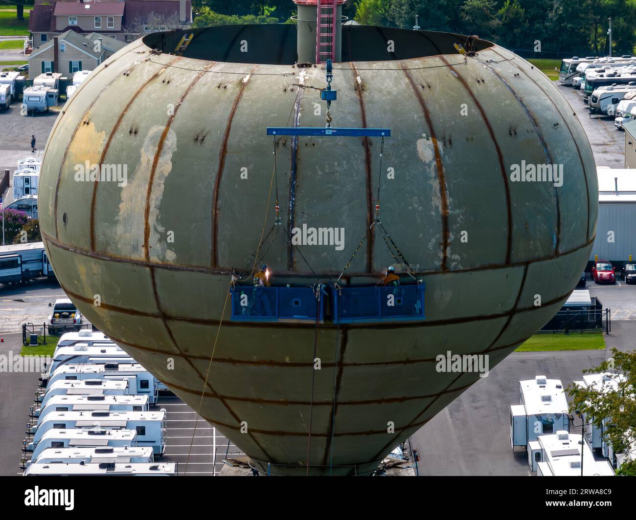 An aerial view of workers welding a rusting old water tower on a cloudy ...