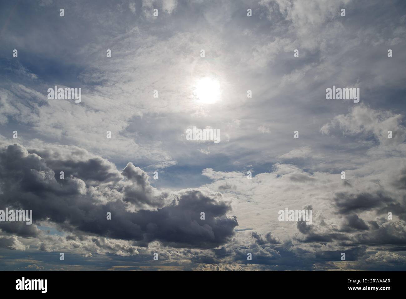 blue sky with sun and mixed clouds on different layers, above horizon ...
