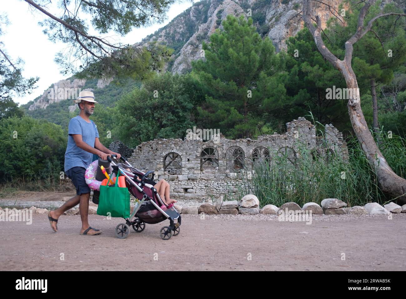 A man pushing a child, buggy, in the ruins of Olympos Stock Photo - Alamy